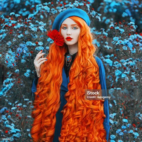 꽃 배경에 파란색 코트에 빨간 머리 여자입니다 손에 빨간 꽃긴 빨간 머리와 패션 모델 터번과 세련된 코트 빨간 입술과 파란 눈 색깔의 손톱 뷰티 초상화입니다 물결 모양의