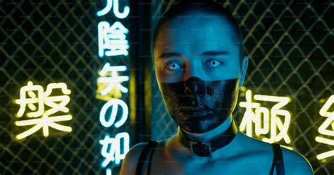 얼굴이 반쯤 검은색으로 칠해진 젊은 사이버펑크 여성이 막대와 조명이 켜진 상형 문자를 배경으로 카메라 앞에 서 있다 사진 Unsplash의 밤 이미지