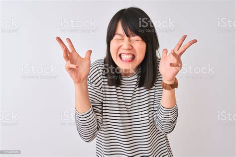 고립 된 흰색 배경 위에 검은 줄무늬 티셔츠를 입은 젊은 아름다운 중국 여성은 팔을 들고 눈을 감고 흥분을 일으키며 성공을 축하합니다 우승자 컨셉 T 셔츠에 대한 스톡 사진