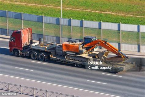 도시의 고속도로에서 긴 트레일러 플랫폼과 교통 트럭에 무거운 새로운 노란색 굴삭기 굴착 기계에 대한 스톡 사진 및 기타 이미지 굴착 기계 나름 2차선 고속도로