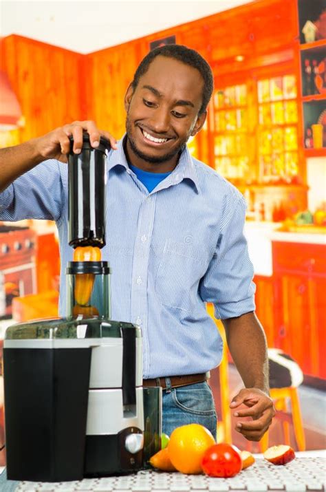 Man Wearing Denim Jeans And Shirt Using Juice Maker Inserting Carrot