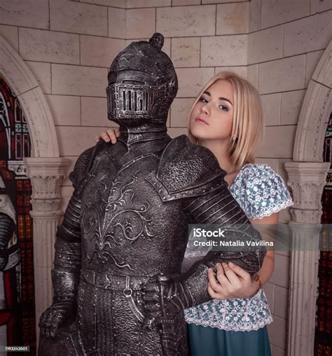 진지한 소녀가 갑옷을 입은 빈티지 기사의 동상 뒤에 서서 손에 들고 카메라를 바라보고 있습니다 남자와 여자의 관계의 개념 검은