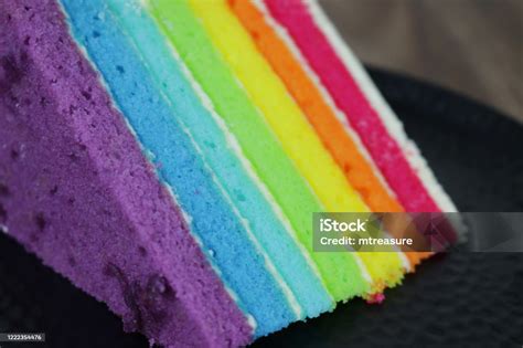 검은 딤플 트레이에 버터 아이싱 크림과 멀티 컬러 스폰지 층 사진을 보여주는 무지개 케이크의 조각의 이미지 레인보우 케이크에
