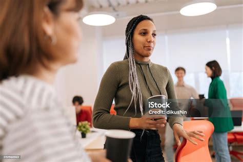 친절한 다민족 동료들이 현대적인 로프트 사무실에 서서 커피 브레이크 동안 비즈니스 문제를 논의합니다 비공식적인 대화를 나누는 남녀 사무실 직원 커피 마실 것에 대한 스톡