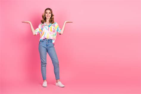 화려한 프린트 셔츠와 청바지를 입은 젊고 쾌활한 여성이 캐주얼 한 분위기에서 장난기 넘치는 제스처를 보여주는 분홍색 배경에 포즈를 취하고 있습니다 20 24세에 대한 스톡