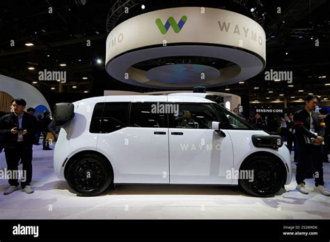 People Look At A Zeekr Rt Vehicle With 6th Generation Waymo Driver On