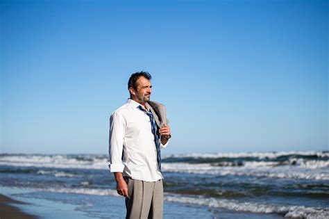 느슨한 흰색 셔츠 블루 넥타이와 그의 어깨에 또는 손에 바다 파도와 함께 해변에 서 있는 중 년 기업 남자의 상체는 배경에서 고독 개념에 대한 스톡 사진 및 기타 이미지