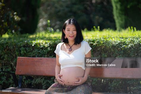 젊은 행복하고 아름다운 아시아 한국 여성 임신 도시 공원 벤치에서 배꼽을 자랑스럽게 여기고 쾌활한 미소를 보여 주면서 임신과