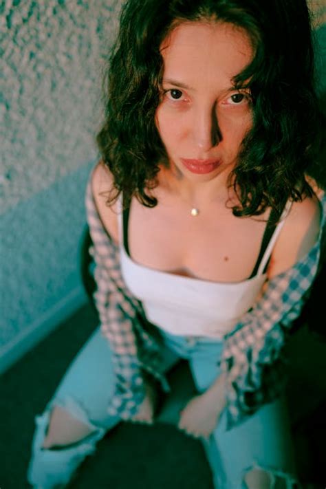 갈색 머리 곱슬머리 나타내는 낮 데님 도시 생활 부드러운 조명 스타일 스타일리시한 실내 설정 앉아 있는 여성 모델 여성스러운 올려다보는 자신감