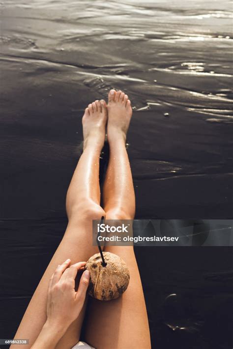 마른 여자는 발리에서 바다 연안에서 코코넛 음료 그녀가 손에 들고 여자 다리 코코넛 일몰에 검은 모래 해변 여름에 감기와 건강 음료 가냘픈에 대한 스톡 사진 및 기타 이미지
