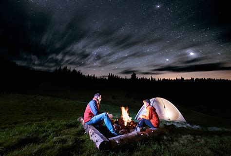 밤 저녁에 캠핑입니다 남자와 여자 관광객 아름 다운 별이 빛나는 밤하늘 아래 조명된 텐트 근처 모닥불에 앉아 텐트에 대한 스톡 사진 및 기타 이미지 Istock