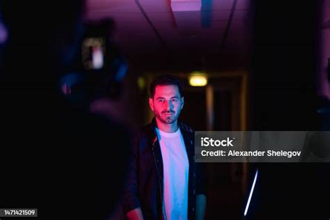 네온 조명을 가진 남자의 남성 초상화 어두운 배경의 빨강 파랑 자주색 및 자홍색 실내에서 어두운 재킷과 흰색 티셔츠를 입는 사람 미래 지향적 인 라이프 스타일 개념 멀티