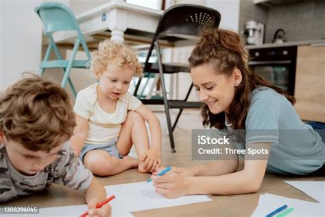 가족은 함께 자유 시간을 보낸다 학교 연령의 아들과 유치원 생딸이 있는 어머니가 집 거실의 나무 바닥에 앉아 있는 동안 함께 모입니다 성인에 대한 스톡 사진 및 기타 이미지