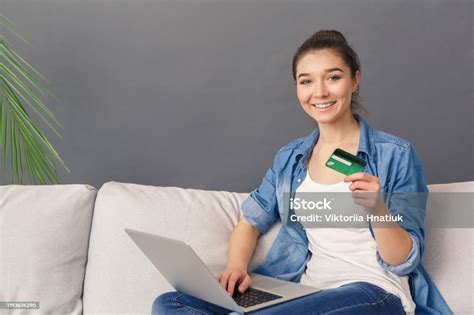 온라인 쇼핑 젊은 여자 앉아 에 소파 스튜디오 고립 에 회색 와 신용 카드 사용 노트북 미소 즐거운 20 29세에 대한 스톡 사진 및 기타 이미지 Istock
