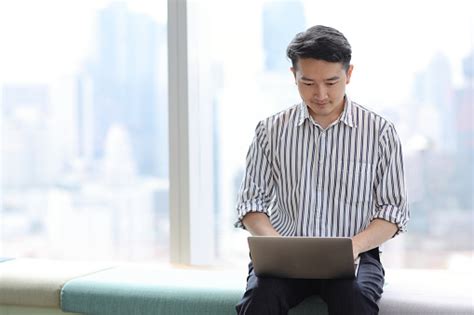 젊은 아시아 사업가가 앉아서 비즈니스 사무실 건물과 도시 배경에서 컴퓨터를 사용하고 있다 25 29세에 대한 스톡 사진 및 기타 이미지 25 29세 건축물 계획