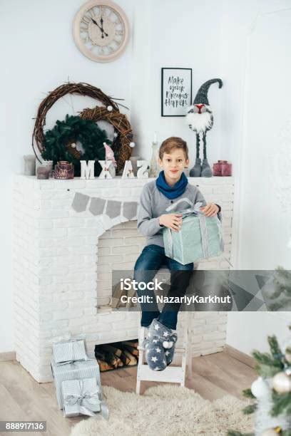 남자 모범생 벽난로에 앉아서 그의 손에 선물 상자를 보유 하 고 공휴일에 대한 스톡 사진 및 기타 이미지 공휴일 깔개 나무 Istock