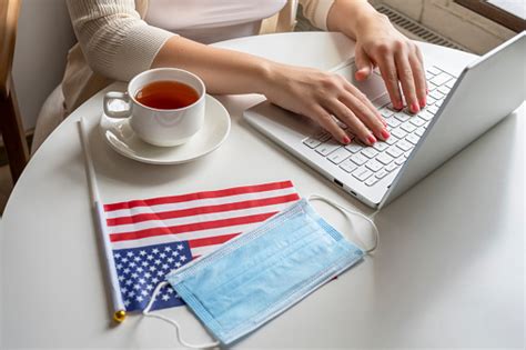여자 관광객 은 노트북에서 일하는 커피 한 잔과 함께 아침 식사를합니다 미국의 국기 카페의 테이블에 의료 보호 얼굴 마스크 공공 장소에서 박테리아와 바이러스로부터 보호 개념