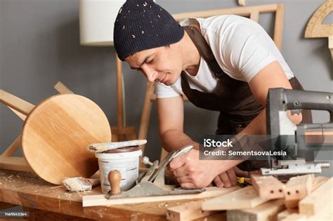 앞치마와 모자를 쓴 잘생긴 남자 목수가 나무 작업장 배경에서 비행기로 작업하고 나무 의자를 만들고 그의 일에 집중하고 참여하는 이미지 35 39세에 대한 스톡 사진 및 기타