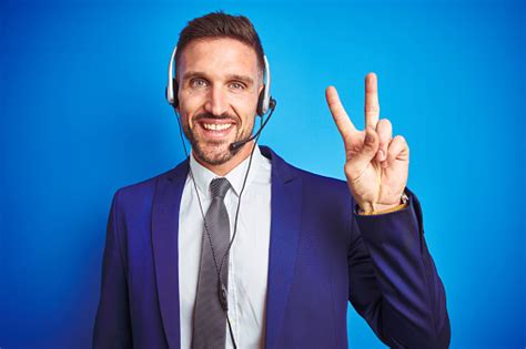 파란색 고립 된 배경 위에 콜 센터 헤드셋을 착용한 젊은 잘생긴 연산자 남자가 승리의 사인을하는 카메라에서 행복한 얼굴 윙크와