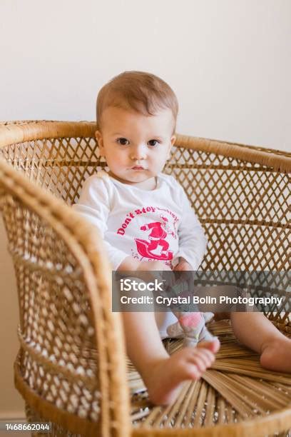 맨발로 등나무 의자에 앉아 티더를 가지고 노는 귀여운 13개월 된 남자 아기 흰색 긴팔 바디수트 아래에 천 기저귀를 차고 Dont Stop Believing이라는 단어가