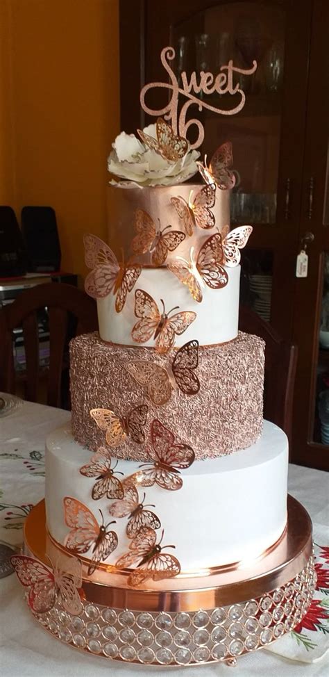 A Three Tiered Wedding Cake With Gold Butterflies On The Top And Bottom