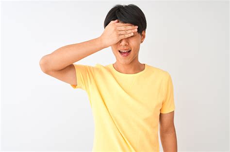 노란 캐주얼 티셔츠를 입은 중국인 남성이 고립된 흰색 배경 위에 서서 미소를 짓고 얼굴을 가린 얼굴을 보며 웃고 있다 블라인드 개념 T 셔츠에 대한 스톡 사진 및 기타