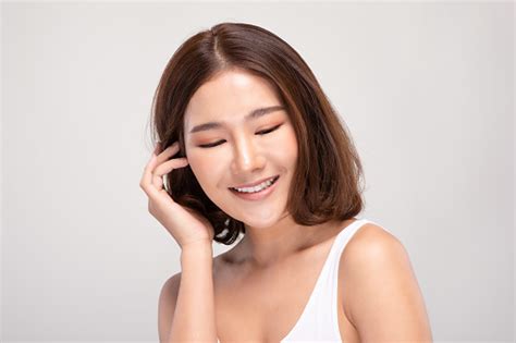 깨끗하고 신선한 피부 행복과 긍정적 인 감정과 명랑 회색 배경에 고립 된 아름다움과 화장품 개념으로 부드러운 뺨 미소를 만지는 아름다운 아시아 젊은 여성 건강관리와 의술에