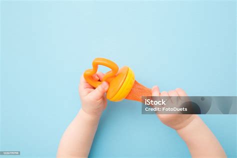 밝은 파란색 테이블 배경에 오렌지 니블러를 들고 유아 손 피더의 그물 자루를 통해 신선한 과일이나 베리를 먹는 아기 액세서리