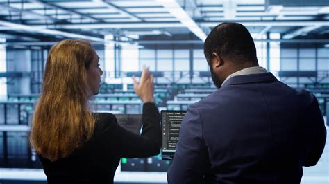 Teamworking Programmers In Data Center Overseeing Server Operations Using Laptop And Tablet