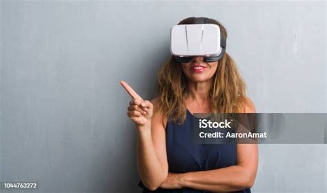 중세 스페인 여자 매우 행복 한 측에 손 및 손가락으로 가리키는 가상 현실 안경을 쓰고 회색 그런 지 벽에 서 3차원 형태에 대한 스톡 사진 및 기타 이미지 Istock