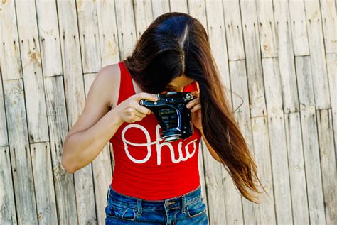 소박한 나무 배경에서 카메라와 함께 포즈를 취하는 빨간색 셔츠와 청바지 반바지에 젊은 아름 다운 갈색 머리 소녀 사진 사진 여자