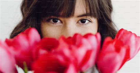 아름다운 갈색 머리 소녀는 실내의 흰색 배경에 빨간 튤립 냄새를 맡고 텍스트를 위한 공간입니다 매력적인 표정을 가진 튤립 사이에 세련 된 젊은 여자 초상화 행복한 여성의
