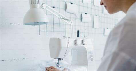 새 옷을 만드는 동안 전기 기계 옆에 앉아 흰색 작업복을 입은 젊은 여성 재봉 공장 노동자 사진 Unsplash의 바느질 이미지