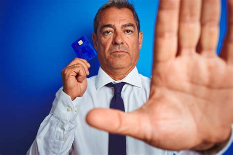 잘 생긴 중년 사업가 는 심각하고 자신감 표정 방어 제스처와 정지 기호를하고 열린 손으로 고립 된 파란색 배경을 통해 신용