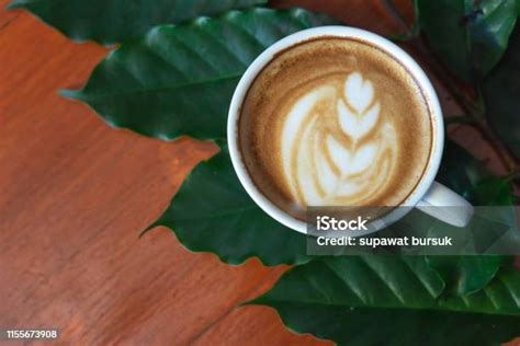 하얀 커피 잔과 커피 원두는 아름 답게 배치 된 나무 테이블에 붓고 커피 잎으로 장식 되어 있습니다 커피를 만들기 위한 원 재료의 혼합물입니다 0명에 대한 스톡 사진 및