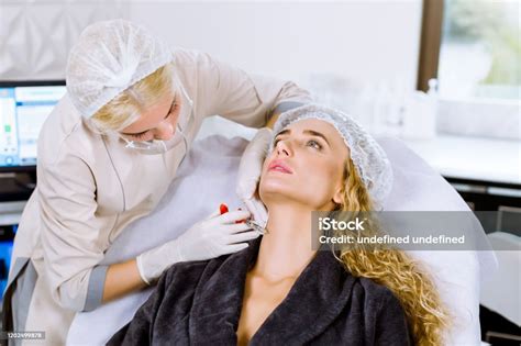 젊은 여성 의사 미용사는 젊은 금발 여성의 얼굴과 목에 주사를 합니다 소녀 도착 아름다움 얼굴 주사 에 살롱 얼굴 노화 회춘 및 수분 공급 절차 2명에 대한 스톡 사진 및