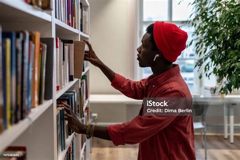 빨간 모자를 쓴 사려 깊은 아프리카계 미국인 학생 남자가 대학 도서관이나 서점에서 책을 고르고 있다 서점에 대한 스톡 사진 및 기타 이미지 Istock