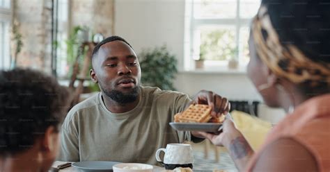 아침에 가족 아침 식사 중에 아내가 들고 있는 접시에서 수제 와플을 꺼내는 동안 식탁에 앉아 있는 젊은 아프리카 남자 사진 Unsplash의 아프리카 계 미국인 가족 이미지