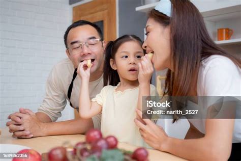 부엌에서 아버지 어머니 딸과 함께 행복한 가족 딸이 집에서 함께 사과 과일을 먹이고 엄마 아빠 아이는 유대감과 관계 생활 방식과 영양 개념을 가지고 있습니다 3 명에 대한