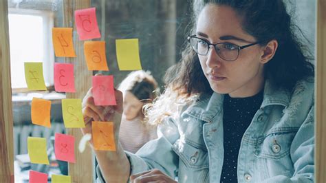 젊은 크리에이 티브 사업가 현대 사무실에서 여성 동료와 함께 일 하면서 프로젝트에 대 한 Glassboard에 색깔된 스티커를 번호 매기기 교육에 대한 스톡 사진 및 기타