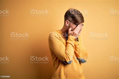 울고있는 동안 손으로 얼굴을 덮고 슬픈 표정으로 노란색 고립 된 배경위에 안경을 쓰고 수염을 기르는 잘 생긴 아일랜드 빨간 머리