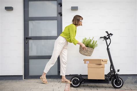 근처에 전기 스쿠터와 소포가 있는 집 현관에서 허브가 든 바구니를 들고 있는 젊은 여성 지속 가능성과 현대적인 친환경 라이프 스타일의 개념 사진 Unsplash의 수송 이미지