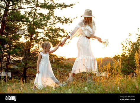 Mother Lead By Hand Little Daughter Through Coniferous Wood At Sunset