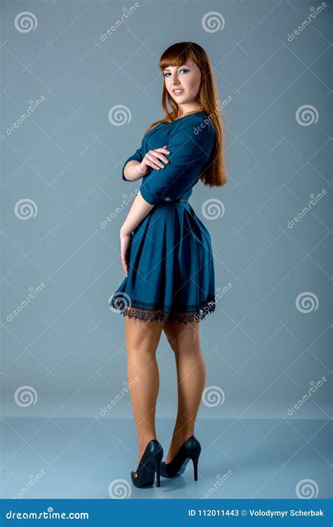 Portrait Of A Plus Size Female Redhead Model Posing In Blue Dress Over Gray Background