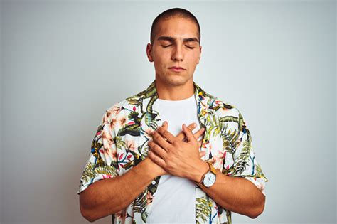 휴일에 젊은 잘생긴 남자는 흰색 배경 위에 하와이 셔츠를 입고 닫힌 눈과 얼굴에 감사 제스처와 가슴에 손을 미소 건강 개념 눈 감기에 대한 스톡 사진 및 기타 이미지