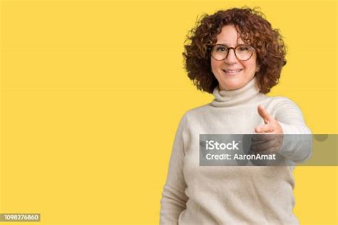 아름 다운 중간 어른 고위 여자 웃 고 인사 하 고 환영으로 제공 하는 친절 한 악수 하는 격리 된 배경 위에 터틀 넥 스웨터와 안경 착용 성공적인 사업입니다 악수에 대한