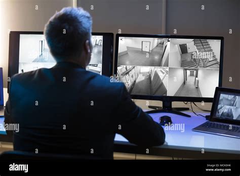Side View Of A Mature Businessman Looking At Cctv Camera Footage On Multiple Computer Screen