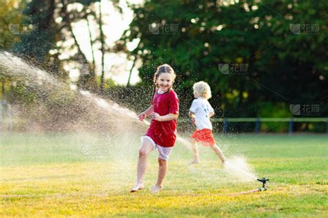 炎热的夏天 孩子们玩水带花园洒水车的儿童户外的乐趣男孩和女孩在水滴训练后跑在足球场上