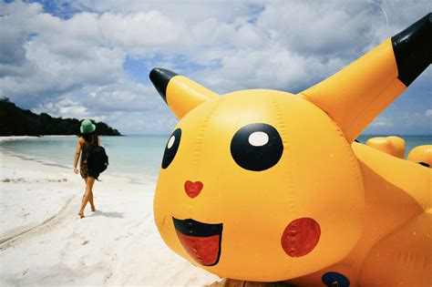 A Woman Walking On A Beach Next To A Large Inflatable Pikachu Photo