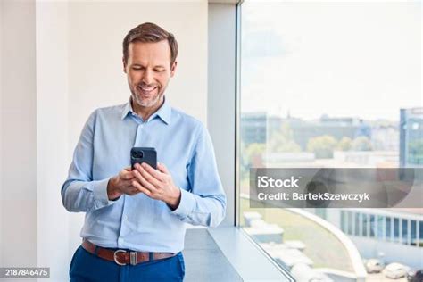 사무실에서 휴대전화를 사용하는 사업가가 창가에 서 있다 40 49세에 대한 스톡 사진 및 기타 이미지 40 49세 Brand Name Smart Phone 경영자